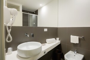 Casa de banho moderna com uma grande lavatório branca, uma lavatório menor, um secador de cabelo e um porta-toalhas.