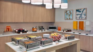 Uma mesa de buffet com diversas opções de comida, micro-ondas e estação de café.