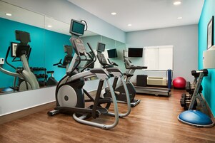 Ginásio com esteiras, pesos e uma bola de exercícios vermelha.