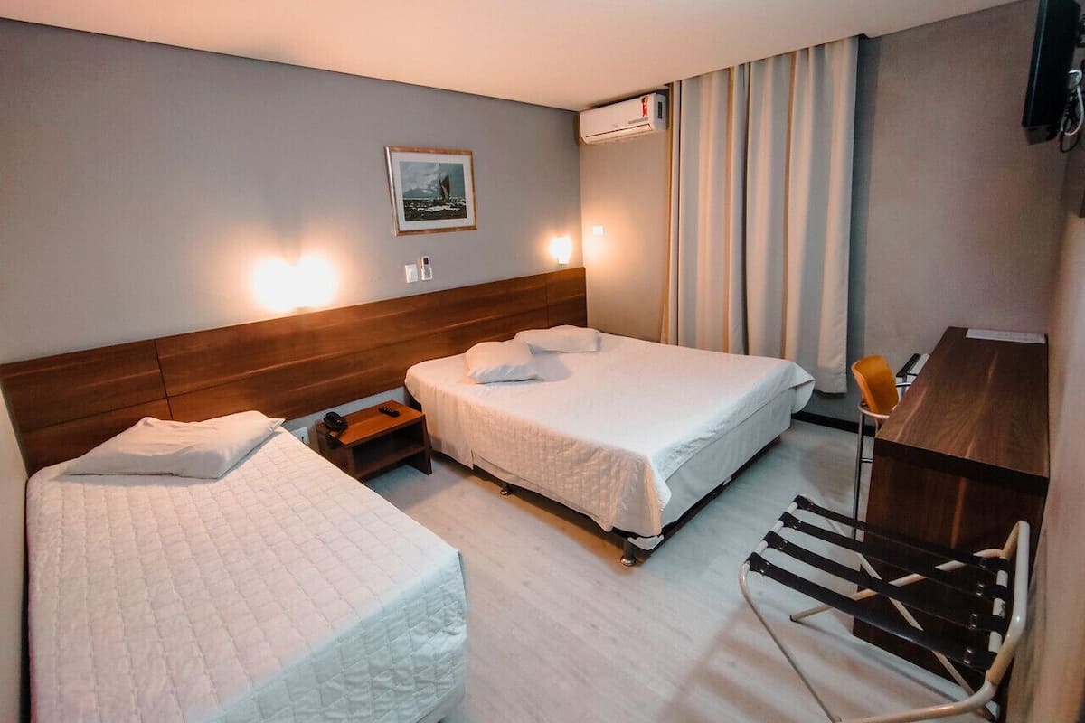 Quarto de hotel com duas camas, uma escrivaninha, uma cadeira, uma televisão e um aparelho de ar condicionado.
