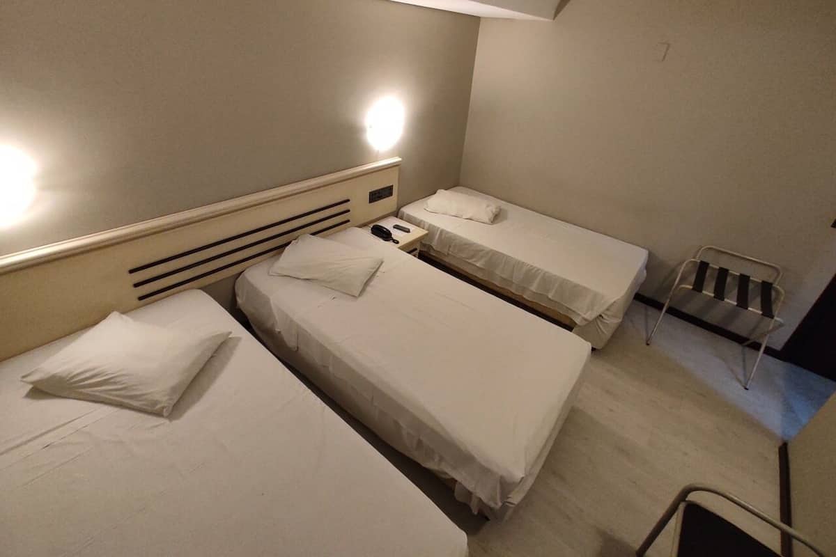 Quarto de hotel com três camas de solteiro, uma mesinha de cabeceira com telefone e uma cadeira.