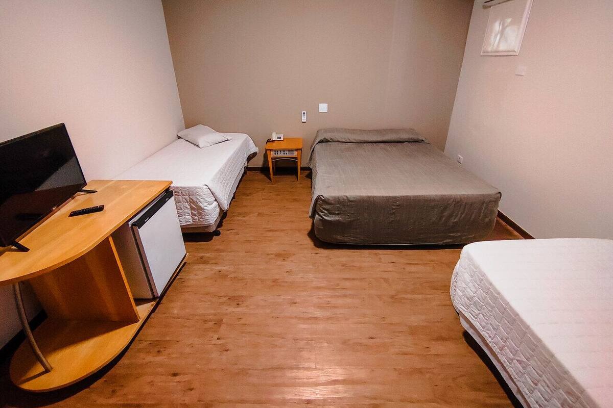 Quarto pequeno e compacto com duas camas de solteiro, uma escrivaninha com cadeira e uma mesinha com telefone.