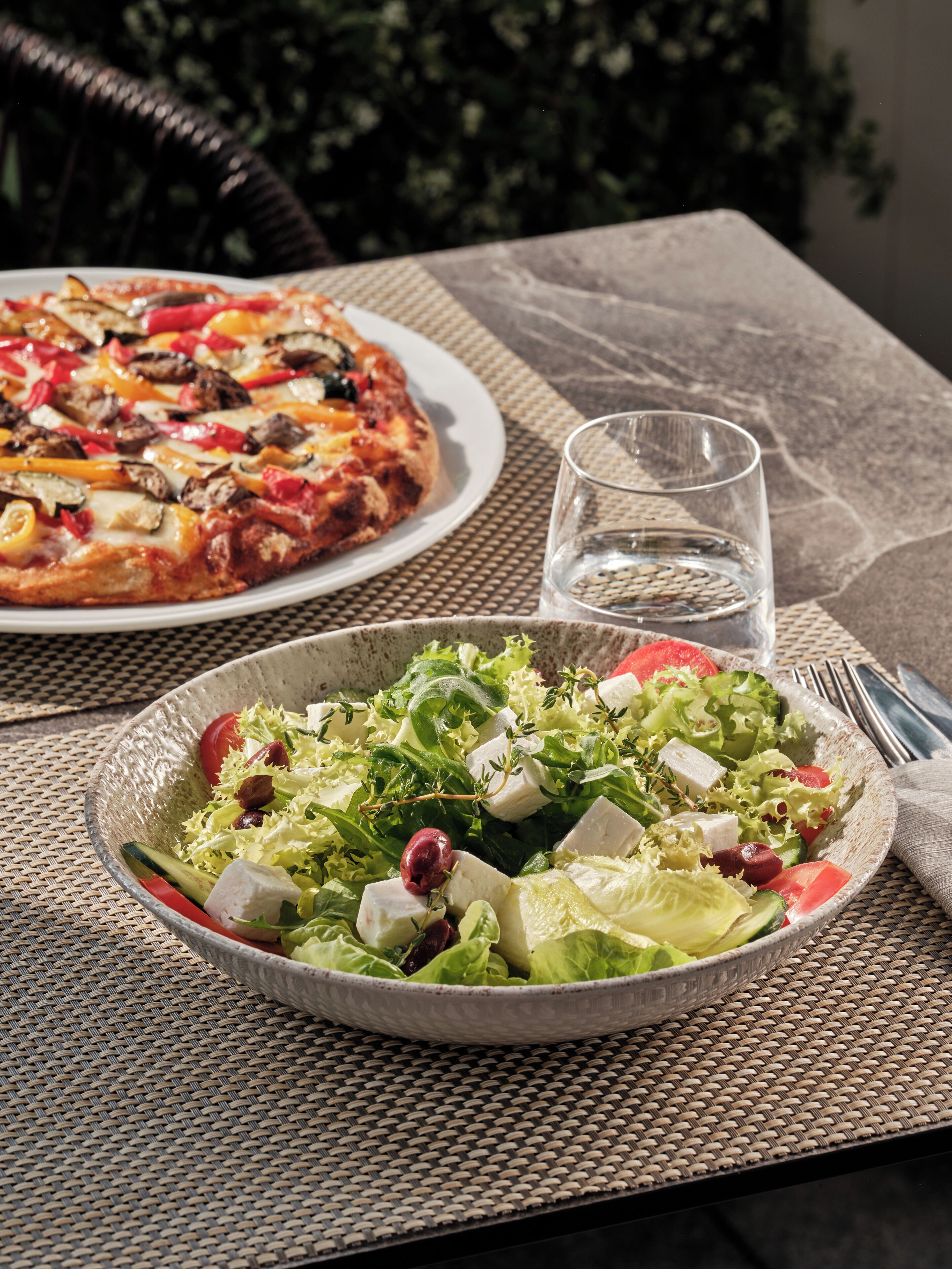 Uma mesa com uma salada num prato, um copo de água e uma pizza.