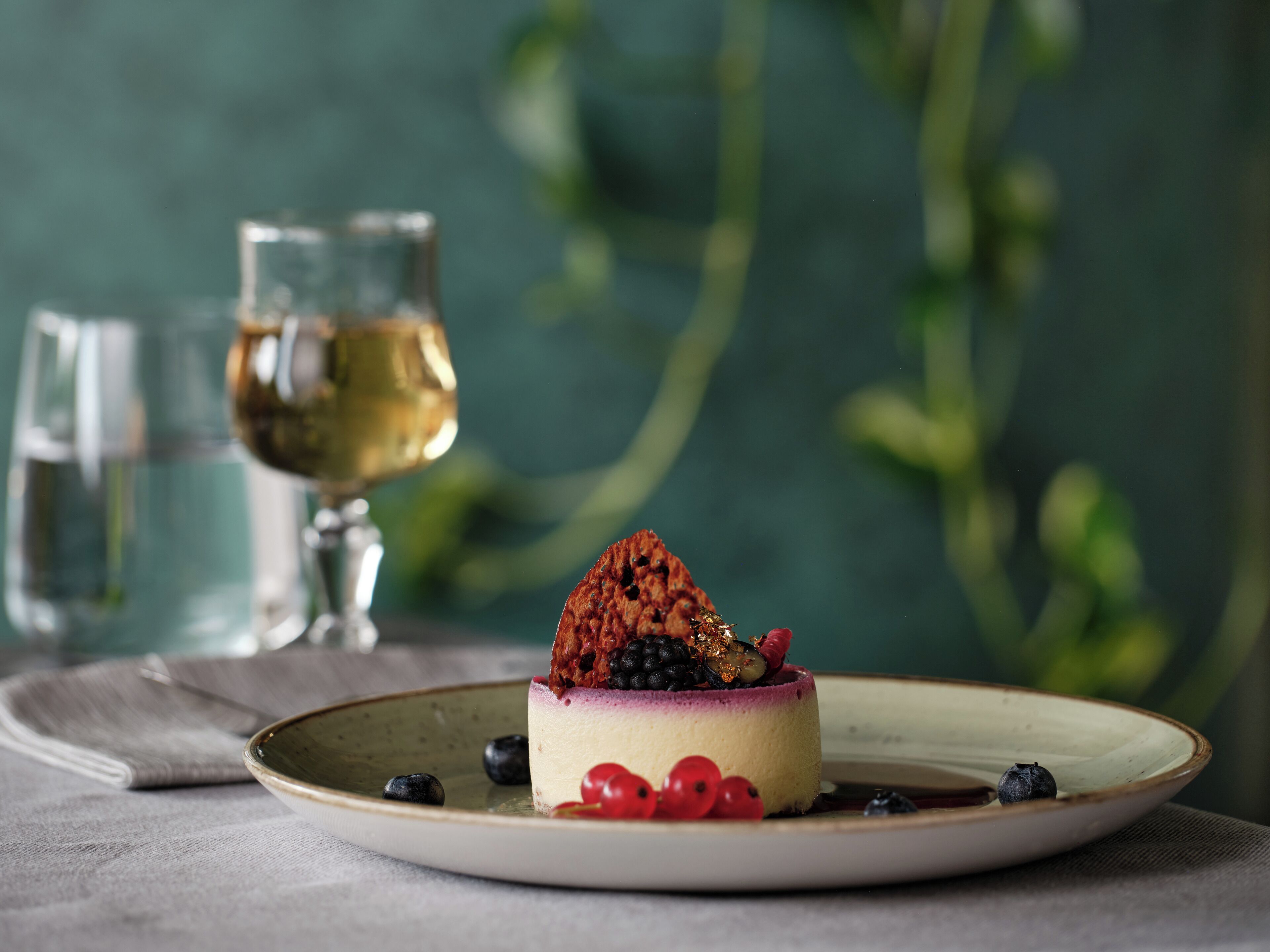Sobremesa em um prato com frutas vermelhas e um copo de vinho ao fundo.