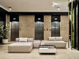 Um lobby moderno com um sofá de canto, uma mesa de centro e dois elevadores.