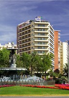 Um hotel com vários andares, uma estátua em primeiro plano e uma fonte.