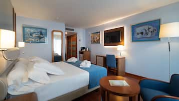 Quarto de hotel com cama, escrivaninha, cadeira, mesa e obras de arte nas paredes.