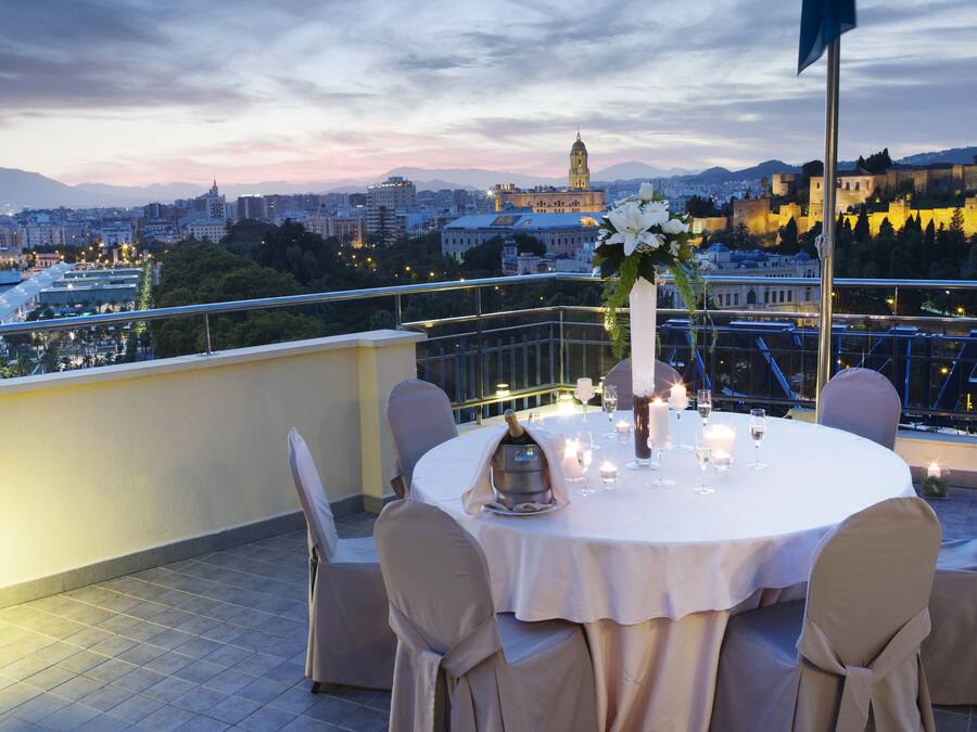 Terraço no telhado com mesa redonda posta para refeições, com vista para uma paisagem urbana com edifícios históricos e um rio.