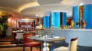 Um saguão de hotel com área de bar, espaços de estar e uma fonte decorativa.