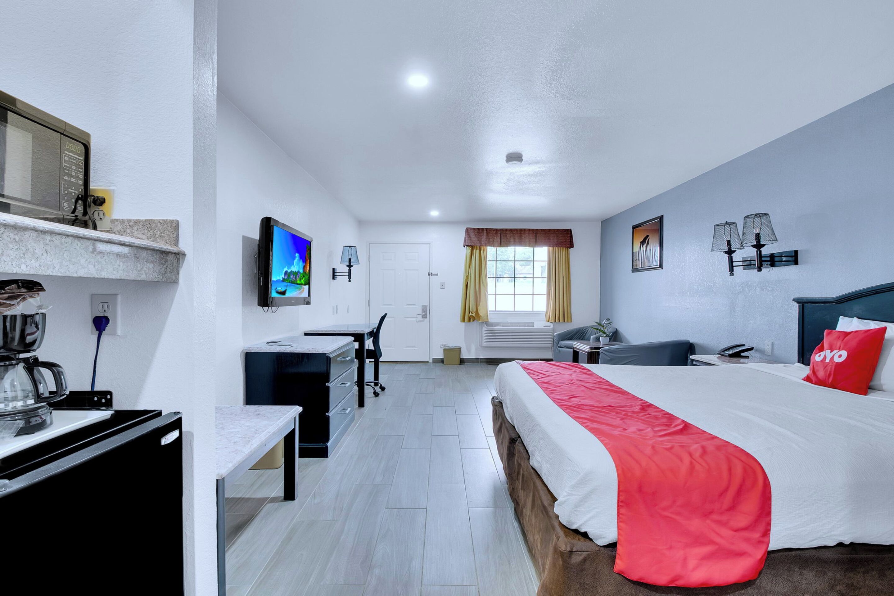 Quarto de hotel com cama, escrivaninha, cozinha compacta e televisão.