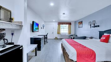 Quarto de hotel com cama, escrivaninha, cozinha compacta e televisão.