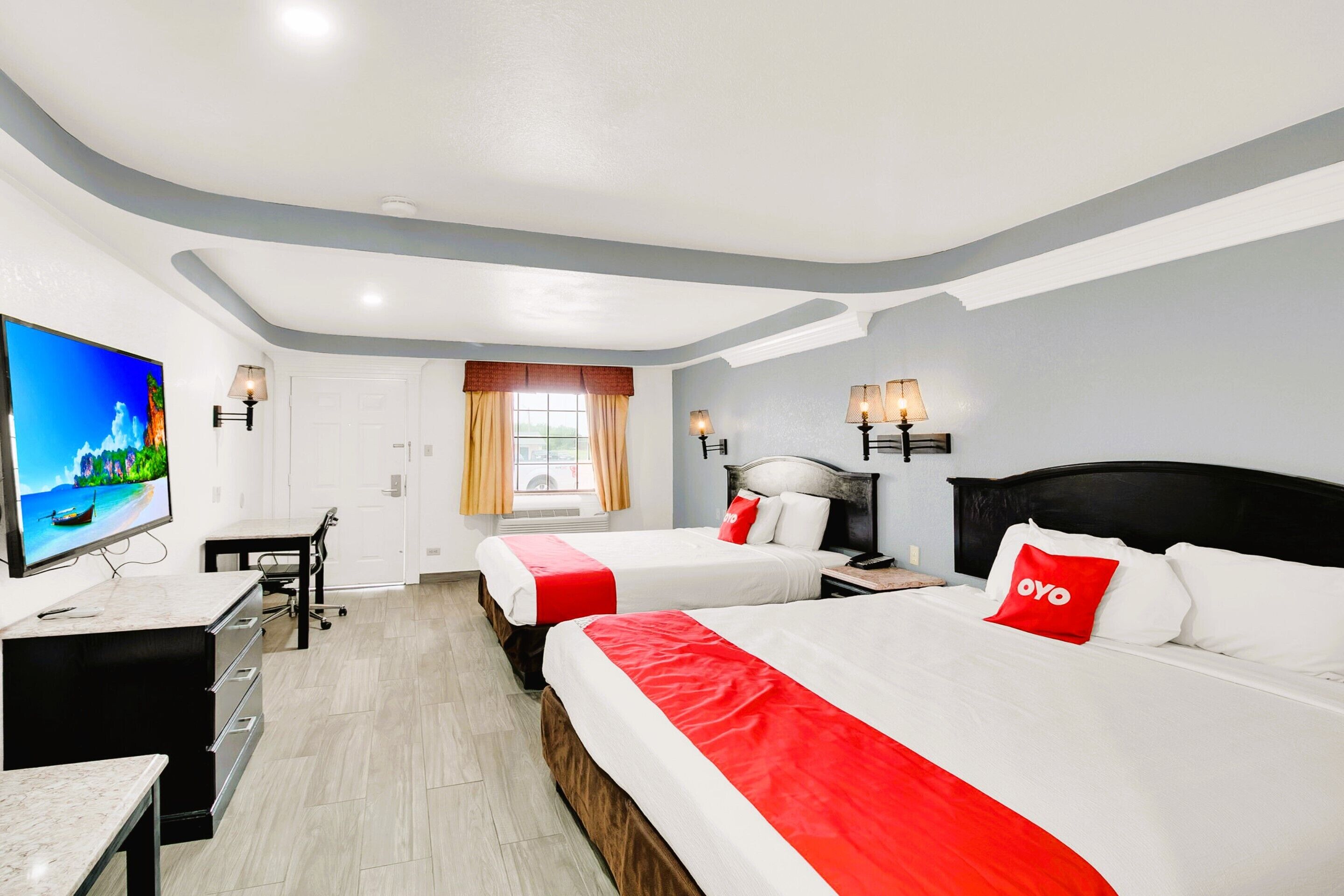 Quarto de hotel com duas camas, uma escrivaninha, televisão e janela com cortinas.