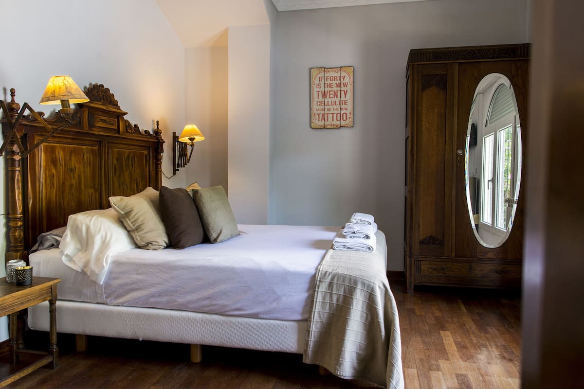 Quarto com cama de madeira, duas luminárias de cabeceira, um espelho e um letreiro na parede.