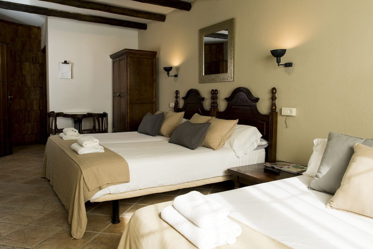 Quarto de hotel com duas camas, um guarda-roupa de madeira, uma escrivaninha e um espelho.