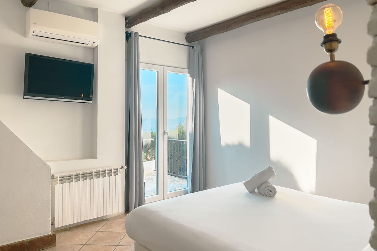 Quarto com cama, televisão na parede, radiador e vista exterior através de uma porta de vidro.