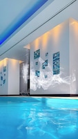 Piscina interior moderna com água azul cristalina, paredes brancas e obras de arte em tons de azul.