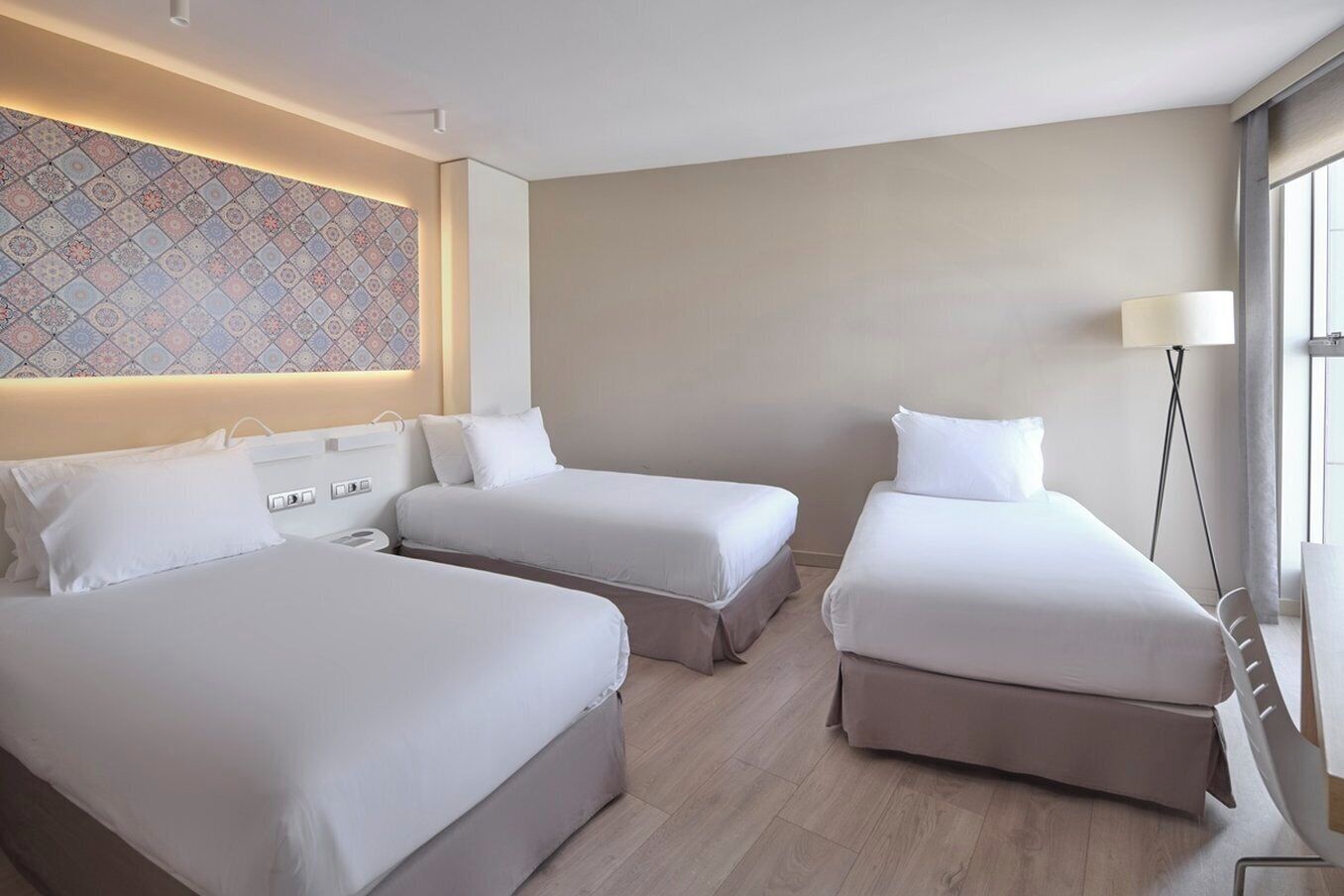 Quarto de hotel com duas camas, uma janela grande e parede estampada.