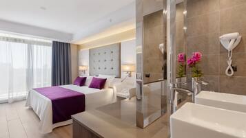 Quarto de hotel moderno com uma cama grande, área de estar separada, banheiro com espelho amplo e vista para a cidade.