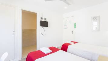 Quarto de hotel com duas camas, um ventilador de teto, televisão e área de chuveiro.