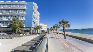 Um hotel à beira-mar com várias varandas, um calçadão à beira da praia e espreguiçadeiras.