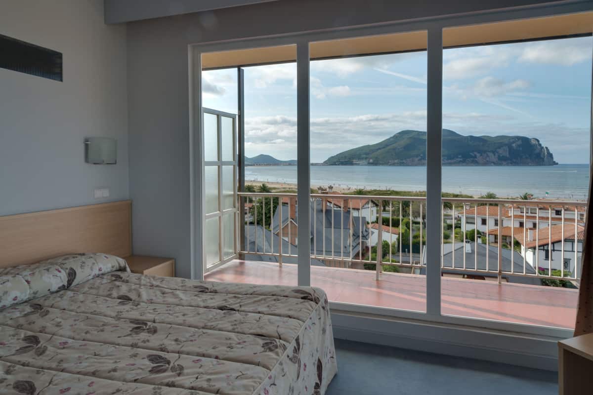 Quarto com uma grande janela com vista para uma praia e falésias.