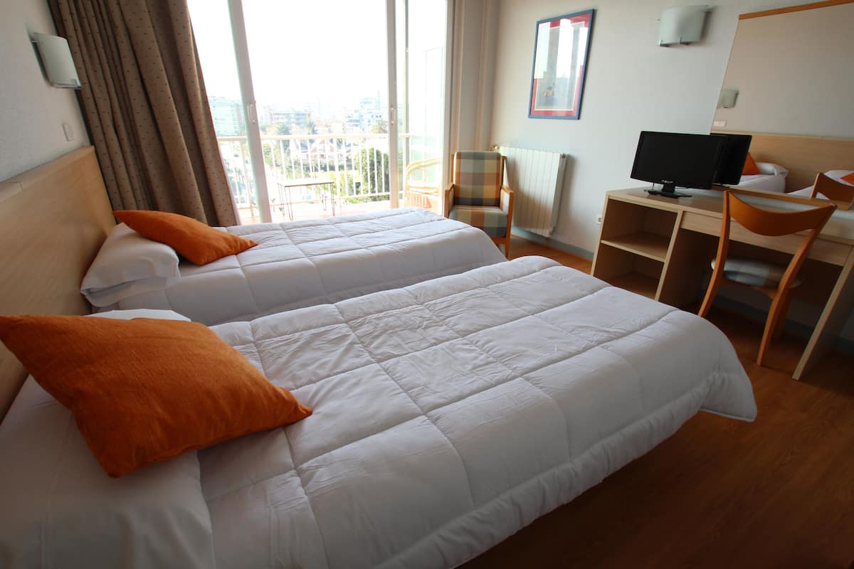 Quarto de hotel com duas camas, uma escrivaninha com computador e uma cadeira.