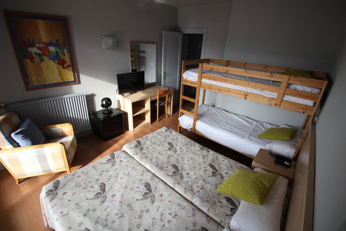 Quarto com uma cama beliche, uma escrivaninha com computador, uma cadeira, radiador e um quadro na parede.