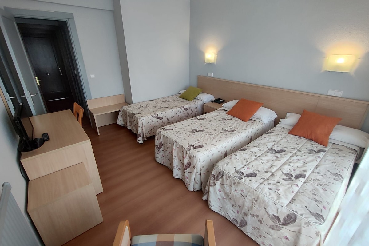 Quarto de hotel com duas camas, uma escrivaninha, uma cadeira e uma porta.