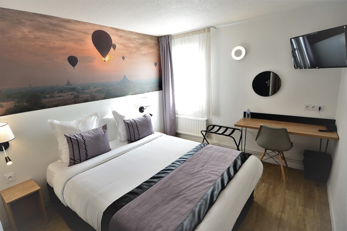 Quarto de hotel com cama, escrivaninha, televisão e pintura de balões de ar quente.