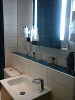 Casa de banho com lavatório branco, espelho, secador de cabelo e porta-toalhas.