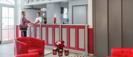 Uma área de recepção com esquema de cores vermelho e branco, uma mesa de centro de vidro com objetos decorativos e uma cadeira vermelha.