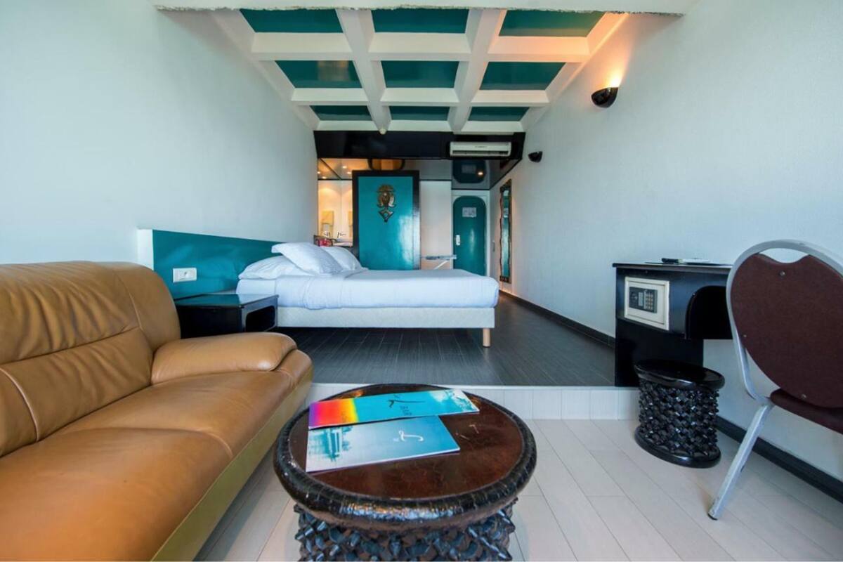 Quarto de hotel moderno com cama, sofá, mesa redonda pequena e escrivaninha com cadeira.