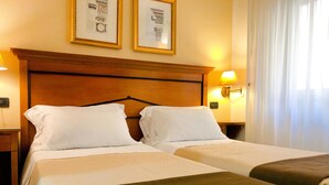 Quarto de hotel com duas camas, cabeceira de madeira, quadros nas paredes e mesa de cabeceira com abajur.
