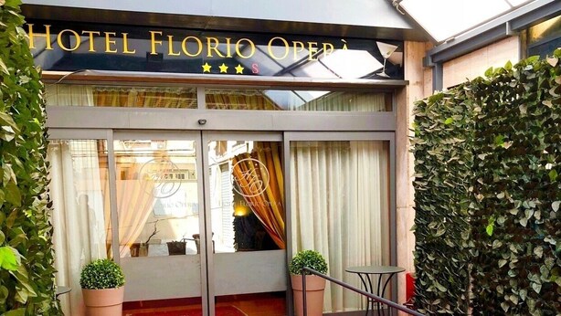 Entrada do Hotel Florio Opéra, com tapete vermelho, plantas em vasos e porta de vidro.