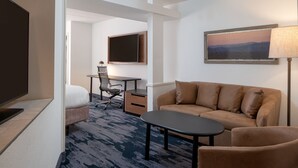 Quarto de hotel com cama, sofá, escrivaninha, poltrona, televisão e um quadro na parede.