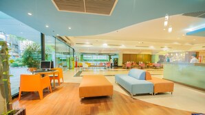 Um saguão de hotel moderno com piso de madeira, balcão de recepção, áreas de estar e grandes janelas com vista para o exterior.