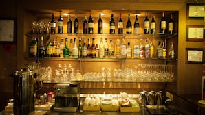 Uma área de bar com prateleiras cheias de garrafas e copos, uma máquina de café e utensílios de cozinha.