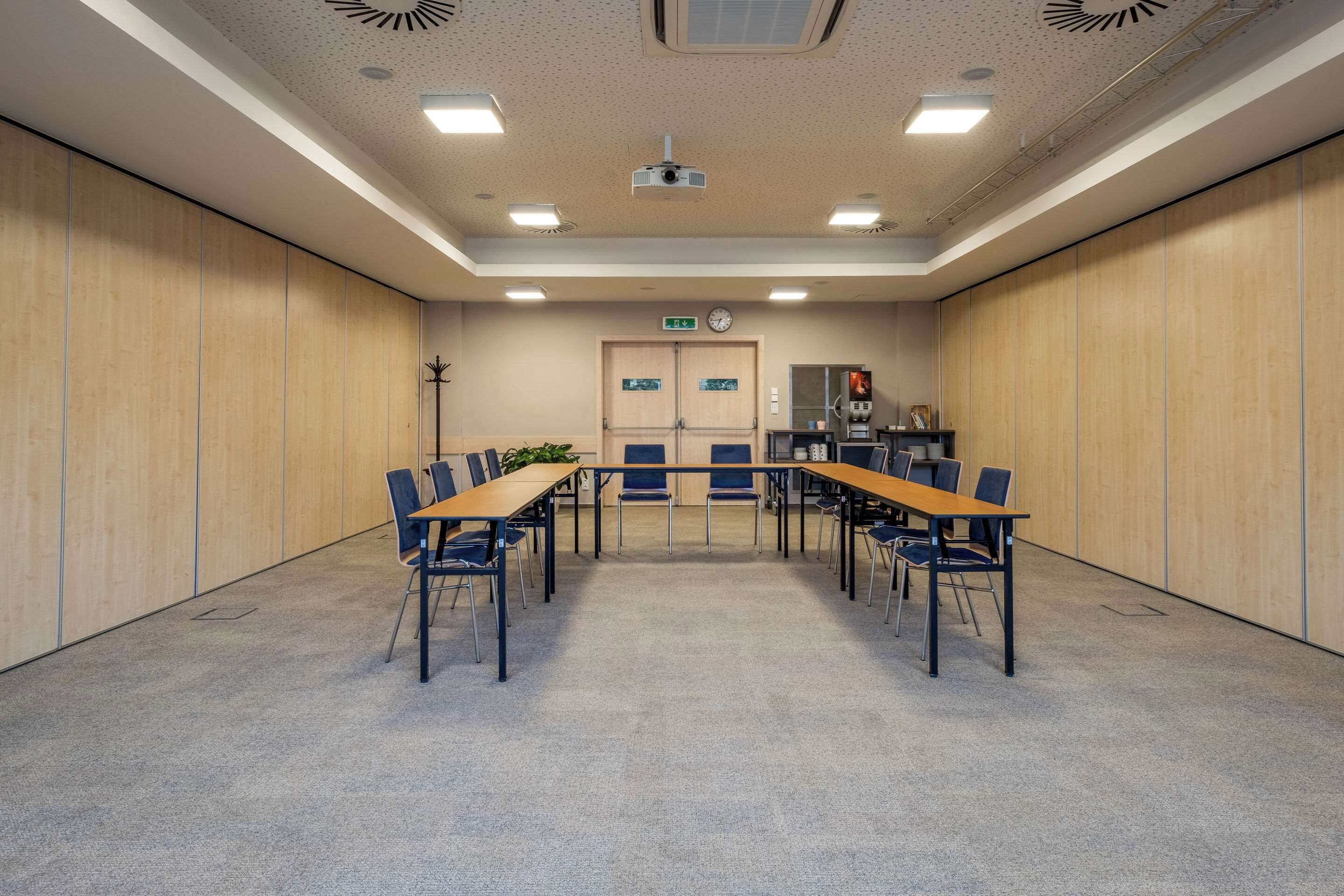 Uma sala de conferência com uma mesa comprida, cadeiras, um projetor e um relógio na parede.