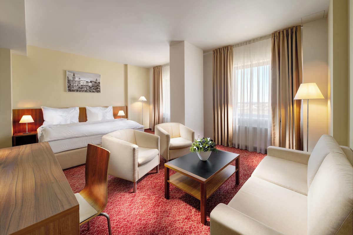 Quarto de hotel com cama, duas poltronas, um sofá, uma mesa de centro e um abajur.