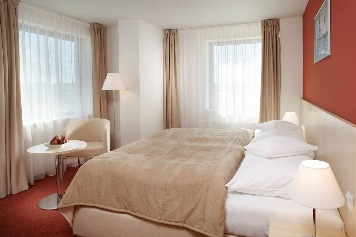 Quarto de hotel com cama, mesa de cabeceira, cadeira e abajur.