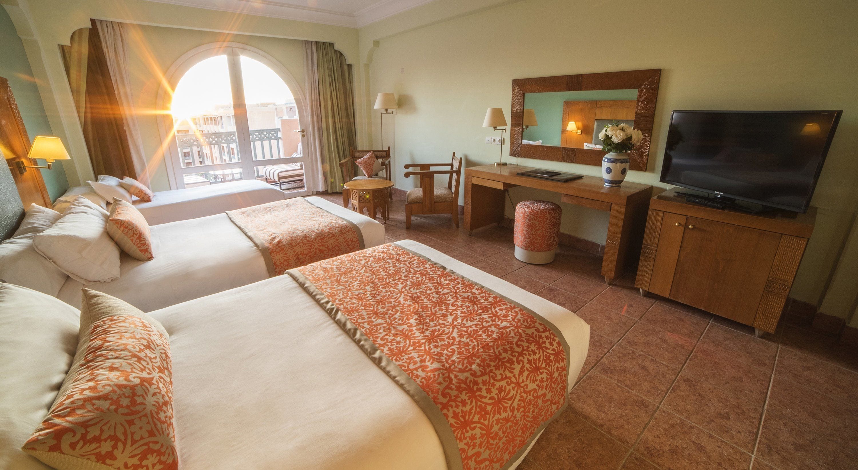 Quarto de hotel com duas camas, uma escrivaninha, uma cadeira, uma televisão e uma janela com cortinas.