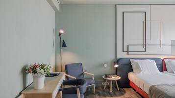 Quarto de hotel com cama, escrivaninha, cadeira, mesinha e abajur.