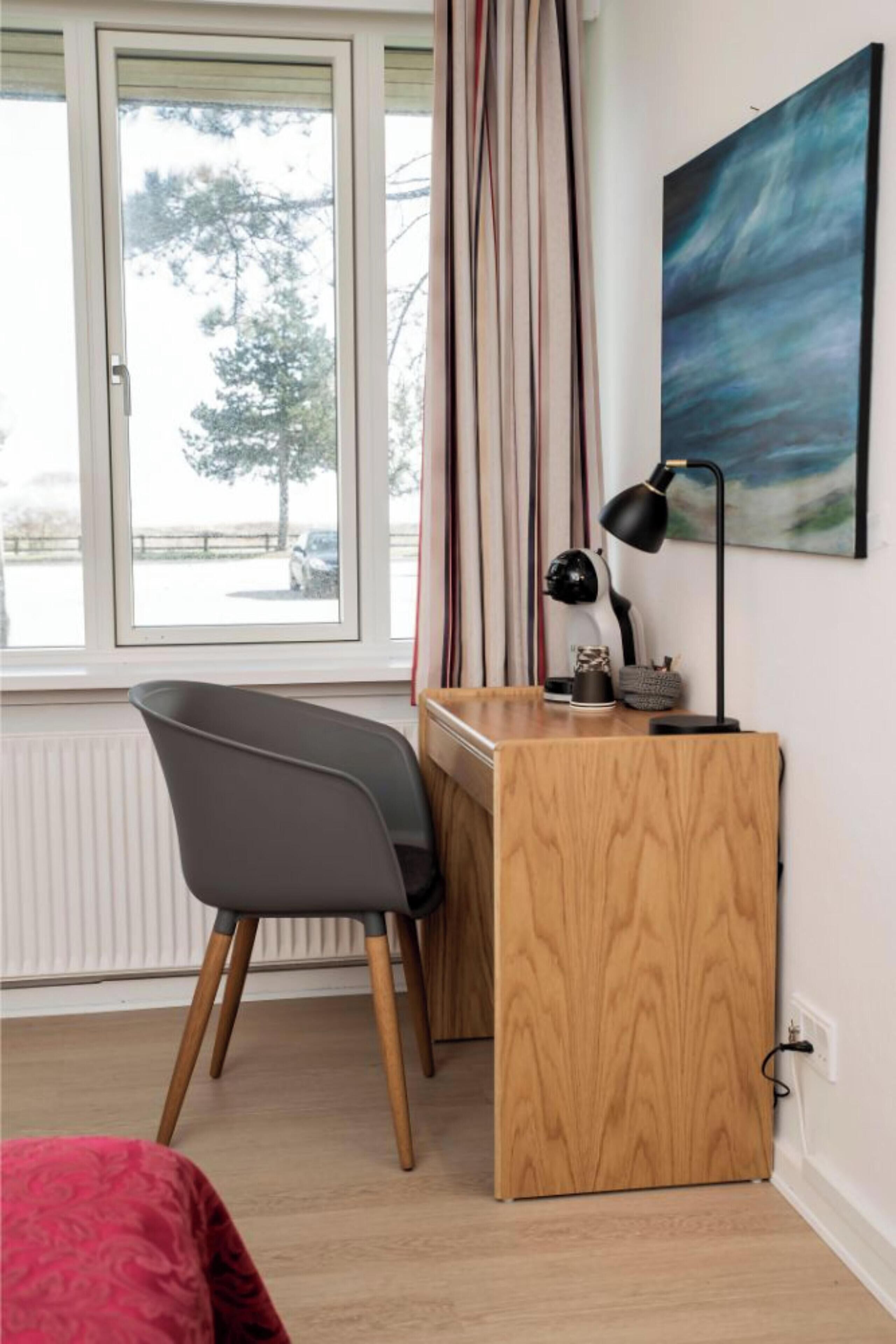 Quarto com escrivaninha, cadeira e janela com cortinas.
