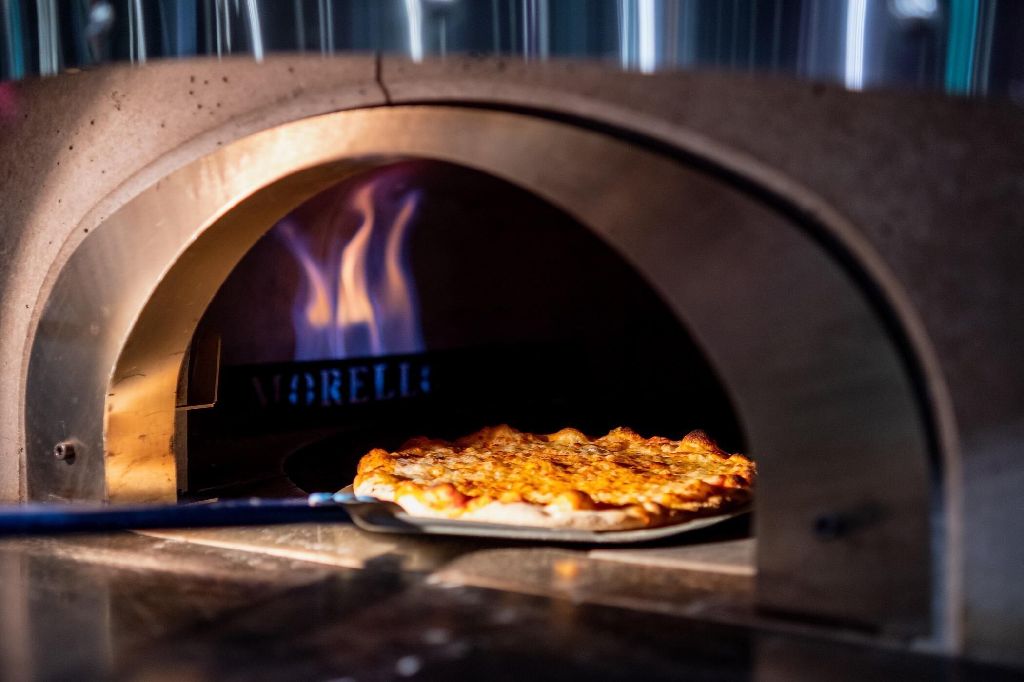 Pizza dentro de um forno a lenha, com chamas visíveis.