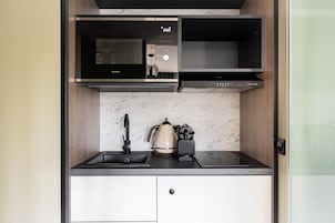 Uma cozinha compacta com micro-ondas integrado, máquina de café e chaleira sobre a bancada.