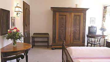 Um quarto com uma cama, um armário de madeira, uma mesinha com uma luminária e uma televisão sobre um criado-mudo.