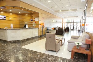 Um hall de hotel com uma receção, área de estar e uma grande janela.