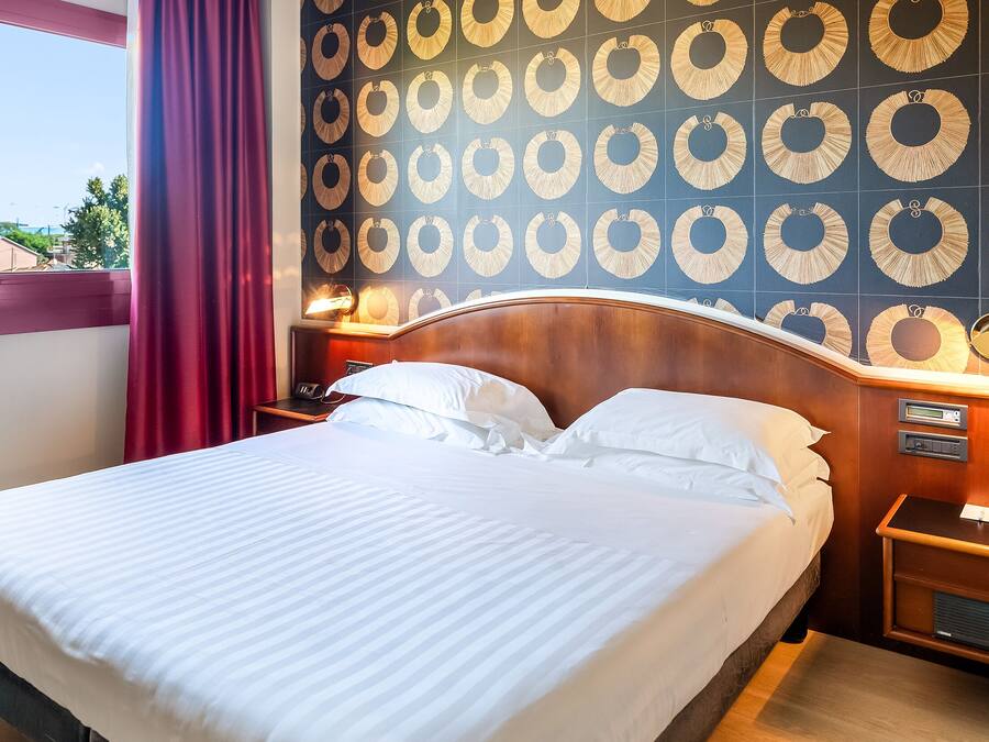 Quarto de hotel com cama, mesa de cabeceira e parede com desenhos circulares.