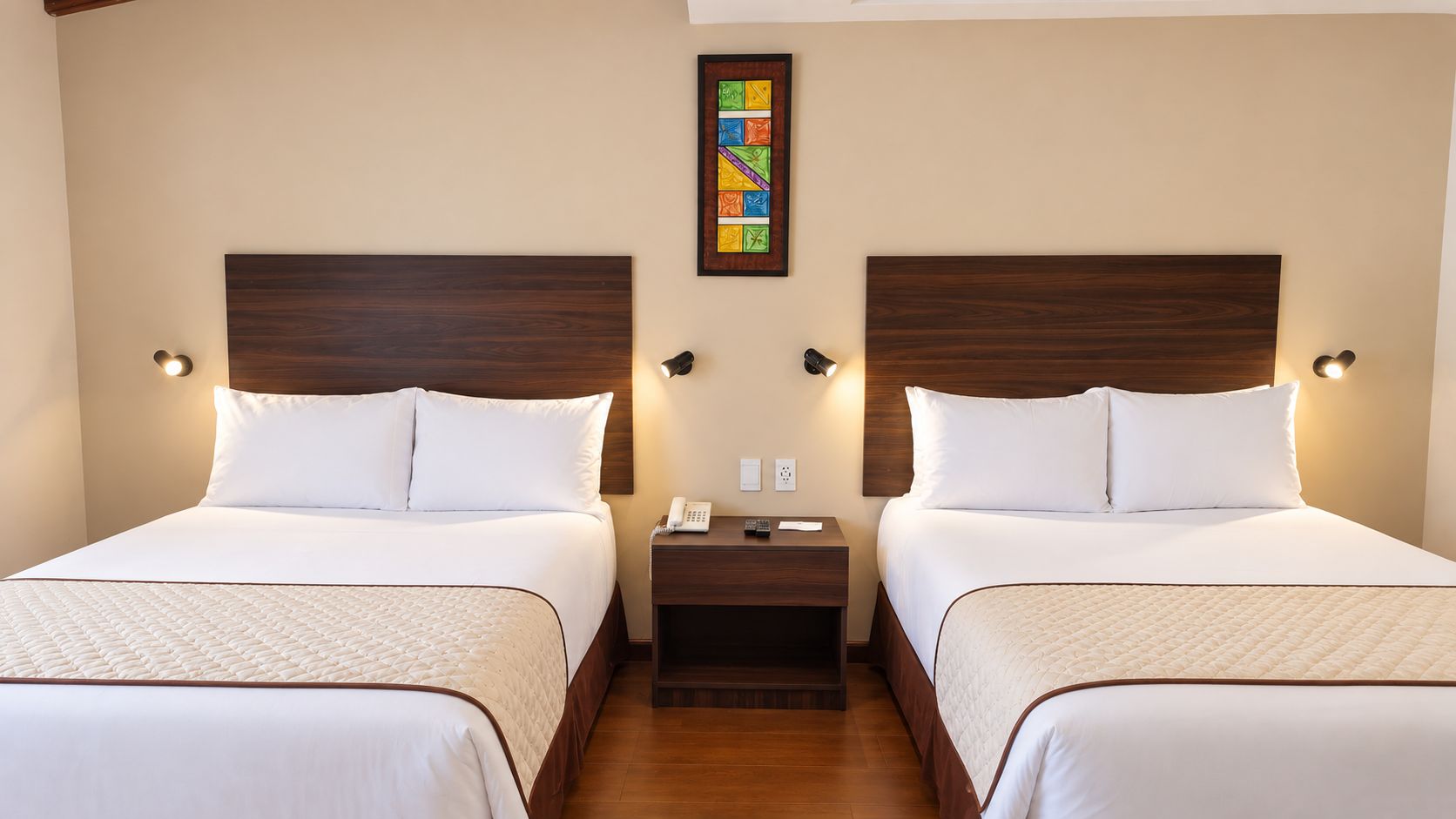 Quarto de hotel com duas camas, uma mesinha de cabeceira entre elas e um telefone fixado na parede.