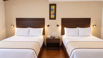 Quarto de hotel com duas camas, uma mesinha de cabeceira entre elas e um telefone fixado na parede.